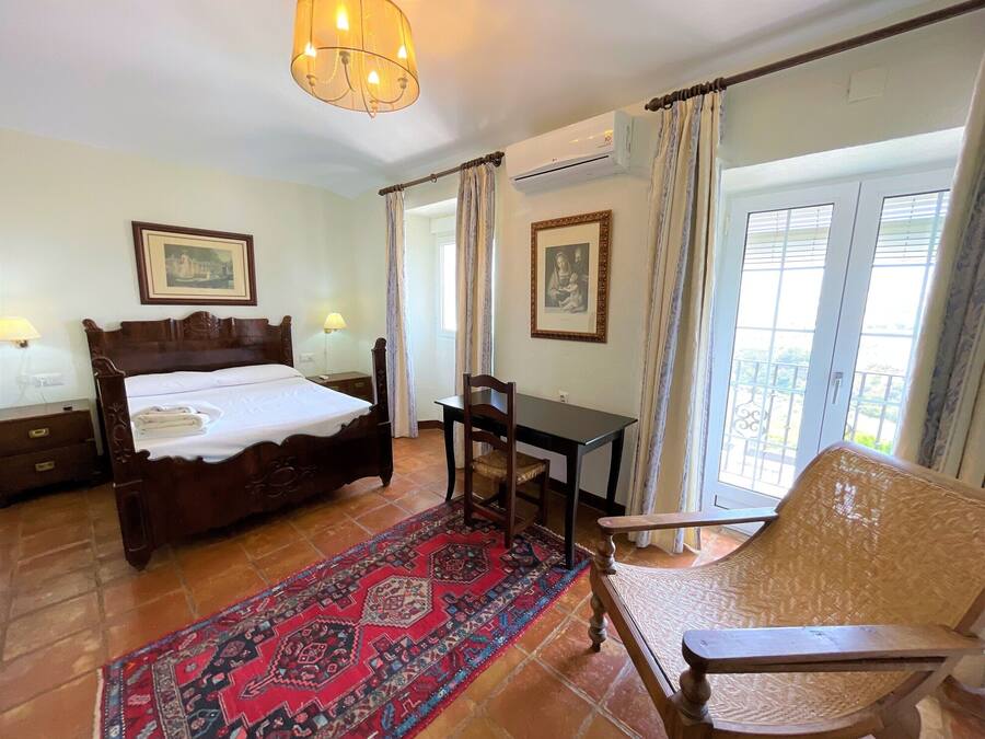 Um quarto com cama de madeira, uma escrivaninha, uma cadeira, um tapete estampado e duas molduras na parede.