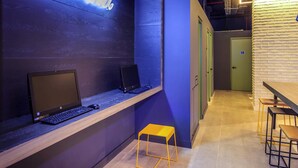 Espaço de trabalho moderno com dois monitores HP sobre uma mesa de madeira, um letreiro de neon com a palavra 'Internet' e um banquinho amarelo.