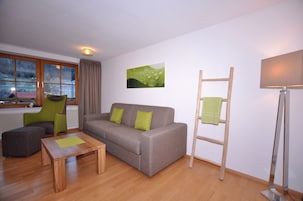 Uma sala de estar moderna com um sofá cinza, almofadas verdes, uma mesa de centro de madeira, uma escada e um quadro na parede.