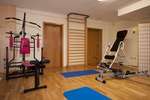 Uma academia com equipamentos de ginástica, piso de madeira e tapetes azuis.