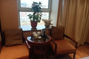 Uma área de estar aconchegante com duas poltronas acolchoadas e uma pequena mesa com um vaso de planta, um tabuleiro com bules e um objeto decorativo.