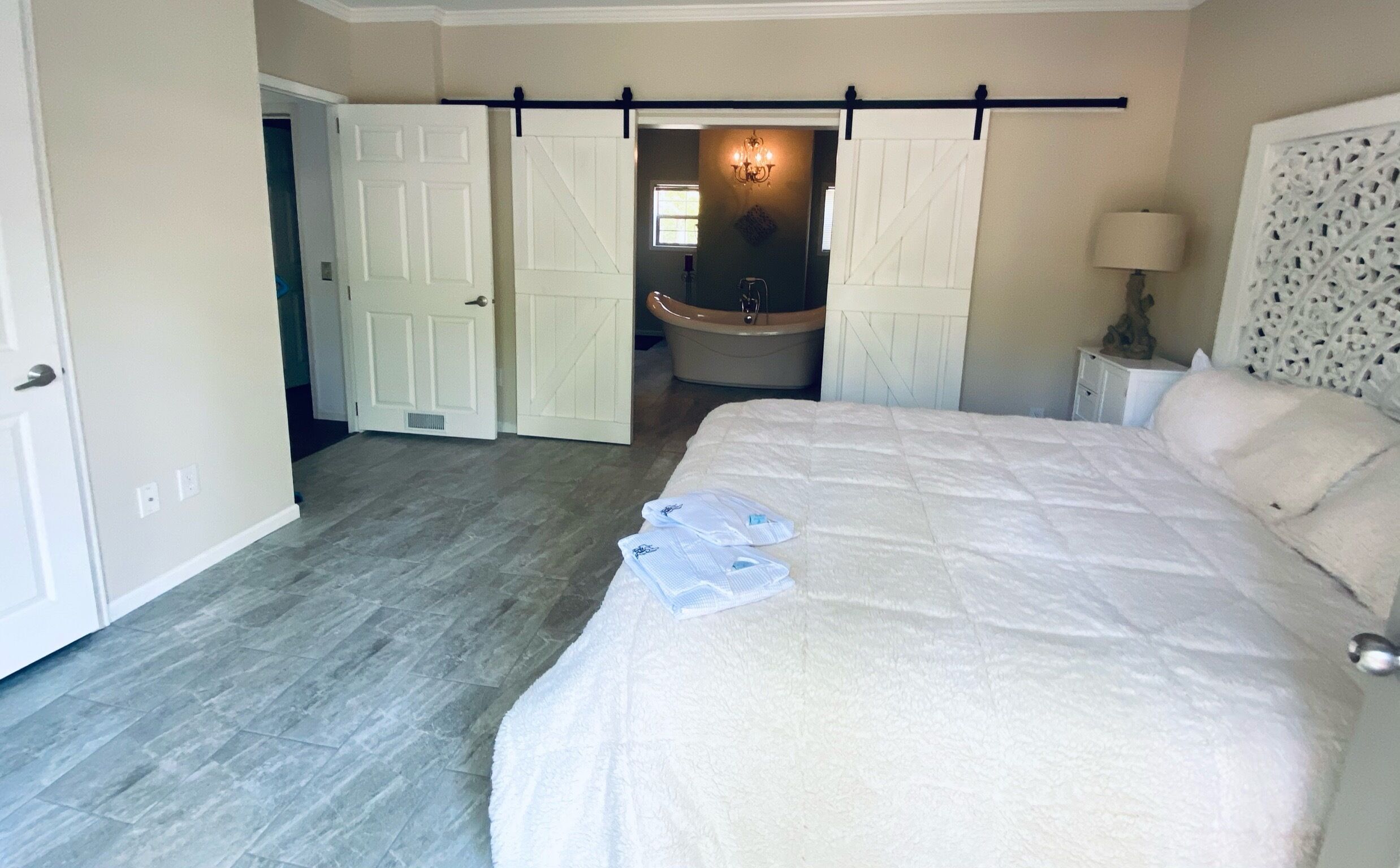 Quarto de hotel com uma cama grande, banheiro com banheira e porta deslizante para outro cômodo.