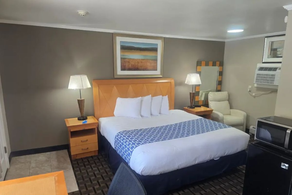 Quarto de hotel com cama, duas mesas de cabeceira com abajures, uma cadeira, escrivaninha e televisão.