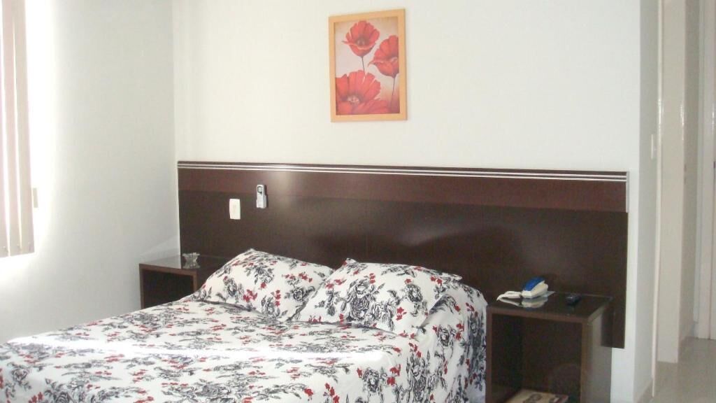 Quarto com cama, mesa de cabeceira, quadro na parede e janela.