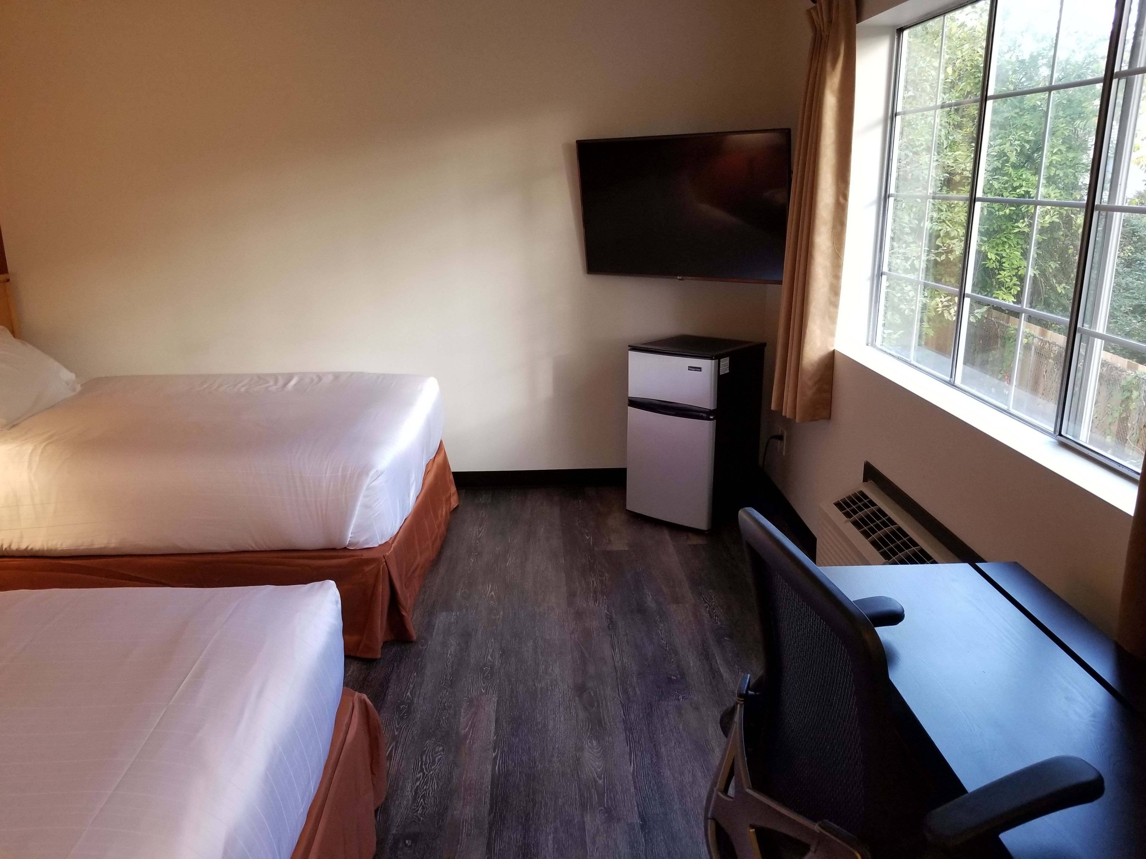 Quarto de hotel com duas camas, uma escrivaninha, televisão e janela com vista para árvores.