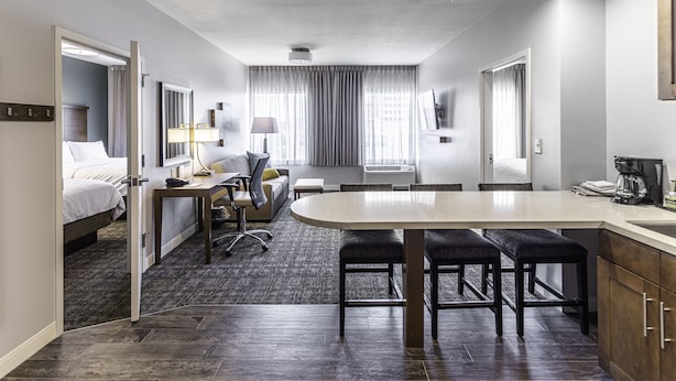 Quarto de hotel moderno com cama, escrivaninha, cadeira e cozinha compacta.