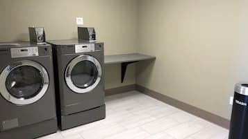 Uma lavanderia com duas máquinas de lavar roupa de abertura frontal e uma lata de lixo.