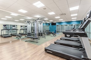 Academia com esteiras, máquinas de peso e colchonetes de exercício.