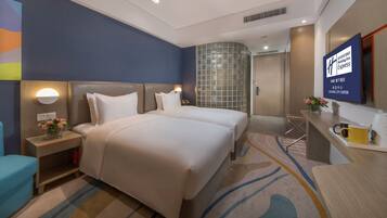 Quarto de hotel com duas camas, uma mesa, uma cadeira, uma televisão e um painel decorativo.