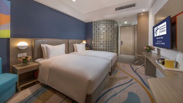Quarto de hotel com duas camas, uma mesa, uma cadeira, uma televisão e um painel decorativo.