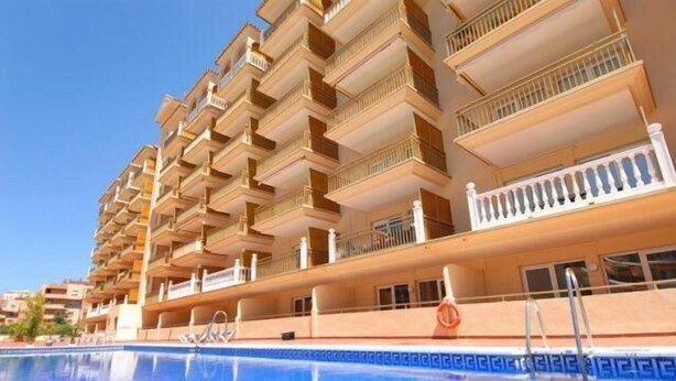 Um hotel com várias varandas, piscina e um céu azul límpido.