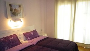 Quarto com duas camas, mesa de cabeceira, luminária na parede e janela com cortinas.
