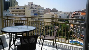 Varanda com mesa redonda e duas cadeiras, com vista para um horizonte urbano com edifícios e piscina.