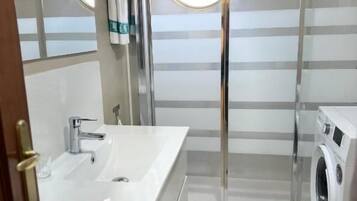 Casa de banho com lavatório, espelho, chuveiro e máquina de lavar roupa.