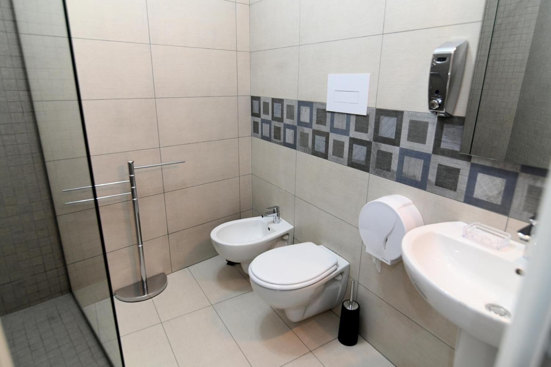 Uma casa de banho moderna com duas sanitas, um bidé, cabine de duche em vidro, uma pia e um dispensador de toalhas de papel.