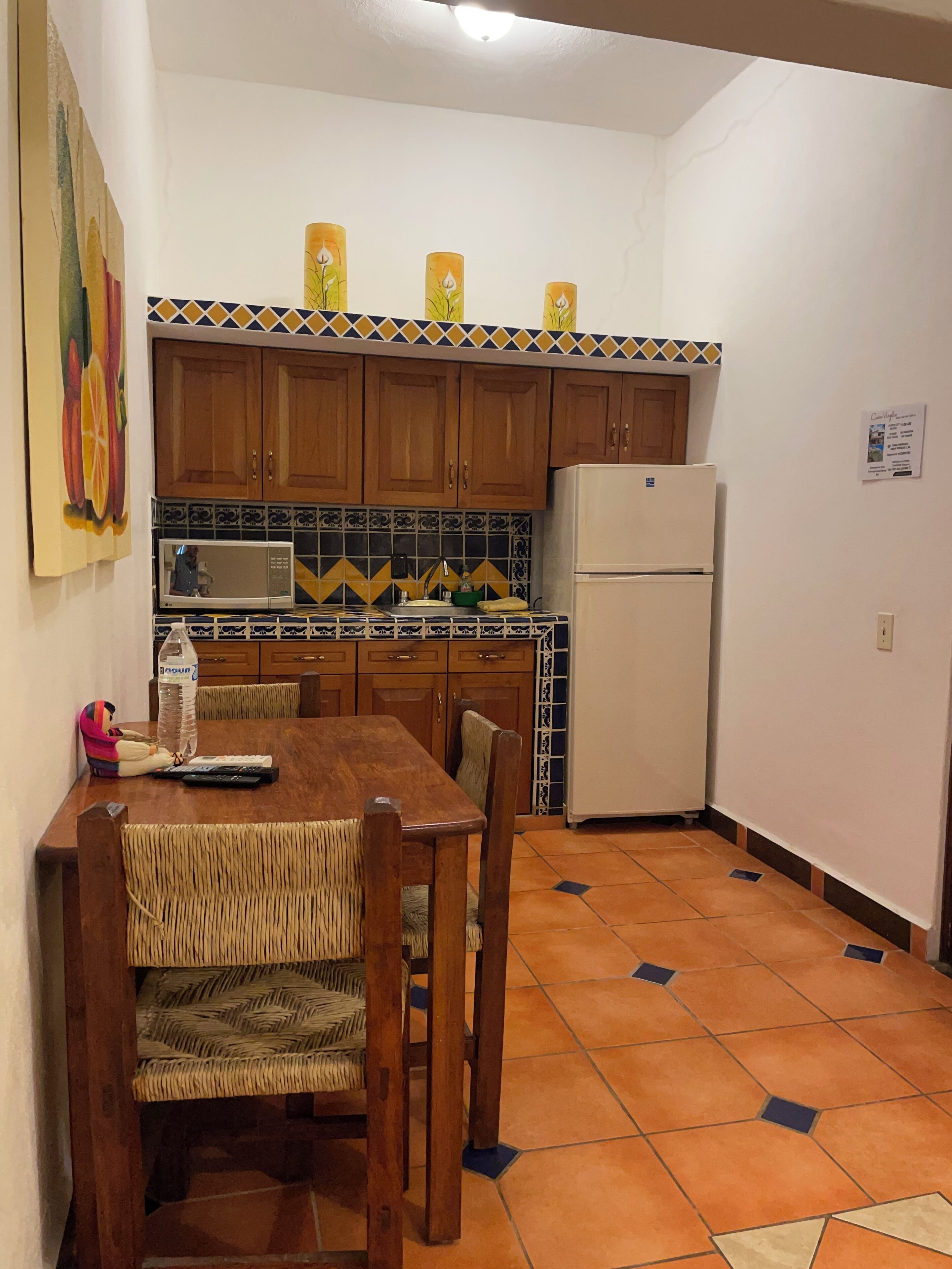 Cozinha compacta com armários de madeira, uma geladeira branca, micro-ondas e uma mesa de jantar com cadeiras.