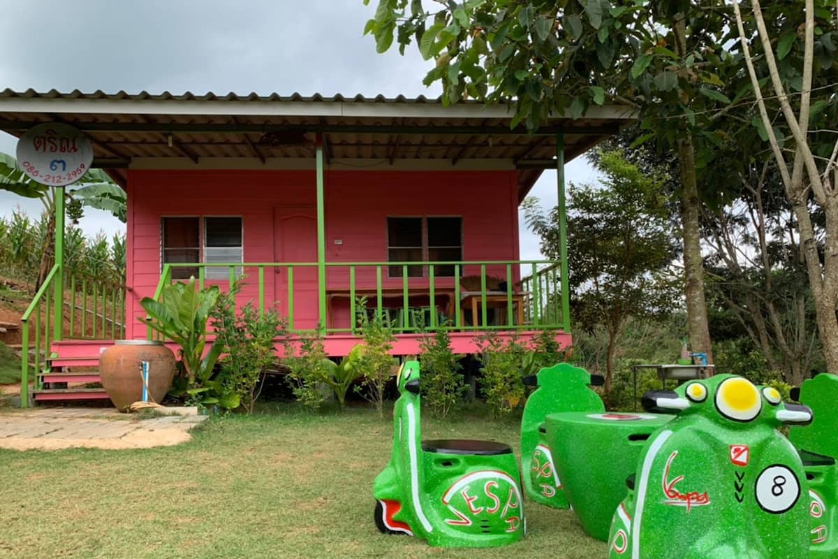 Uma casa rosa com varanda verde e um vaso grande nos degraus.
