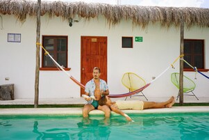 Um casal relaxando em uma piscina com uma rede, uma porta de madeira e um telhado de palha.