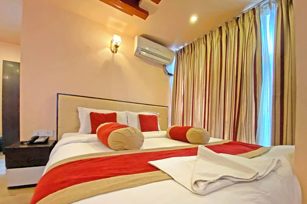 Quarto de hotel com uma cama grande, almofadas vermelhas e bege, telefone ao lado da cama e aparelho de ar condicionado.