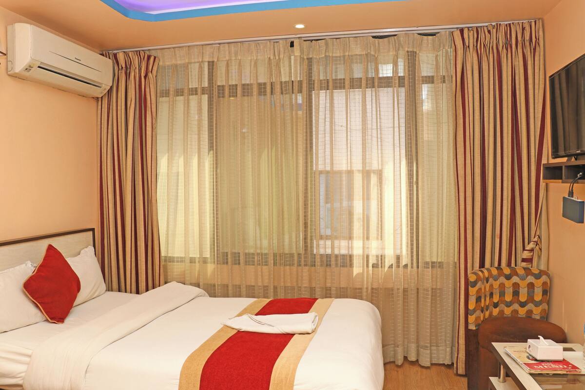 Quarto de hotel com cama, cortinas, televisão e secretária com cadeira.