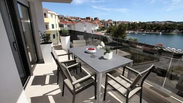 Uma varanda com mesa e cadeiras, com vista para um corpo d'água e uma cidade.