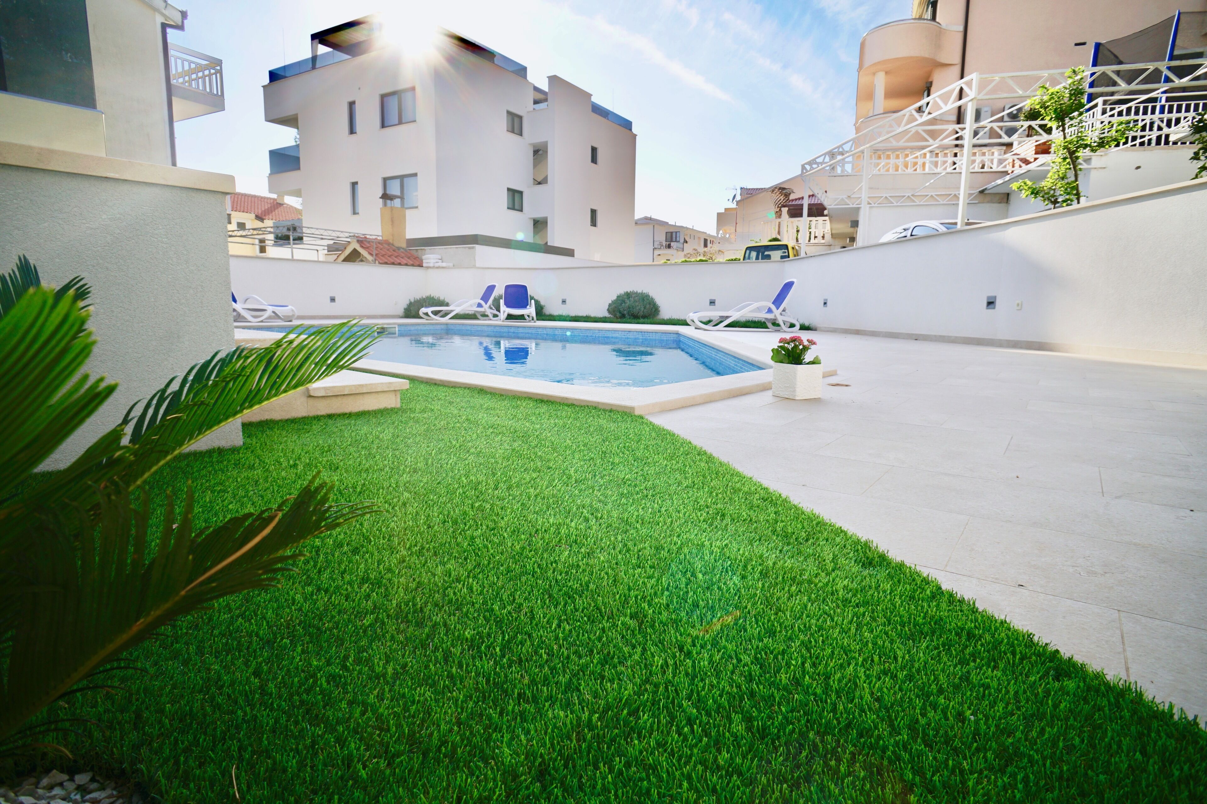 Uma área de piscina moderna ao ar livre com grama sintética, cadeiras de descanso e um pequeno jardim.