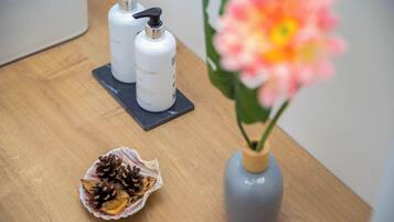 Uma mesa de madeira com duas garrafas brancas, um pinhão em um copo de papel e um vaso com uma flor.