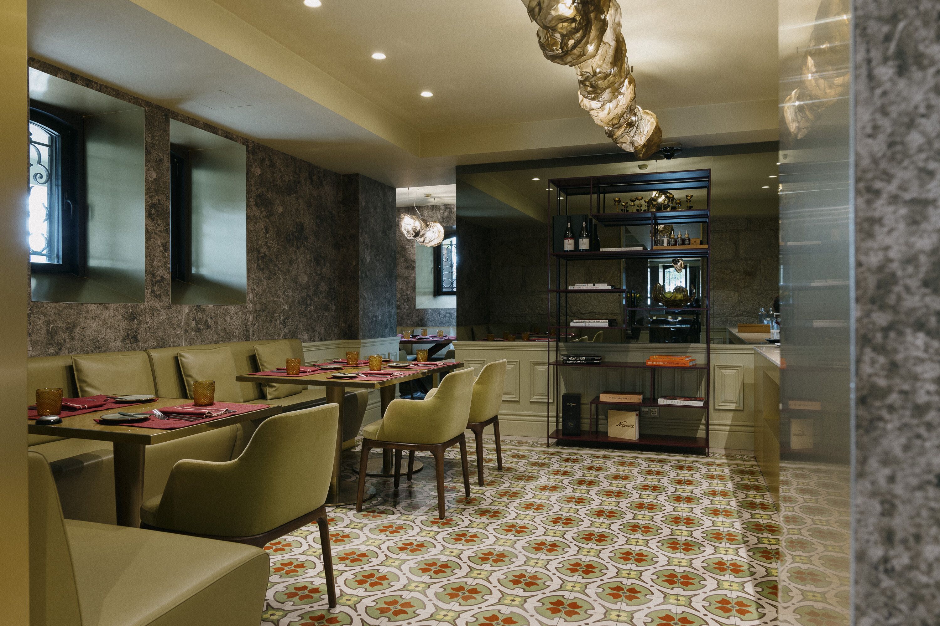 Um restaurante com interior moderno, apresentando um piso estampado, assentos acolchoados e um bar com prateleiras exibindo garrafas.