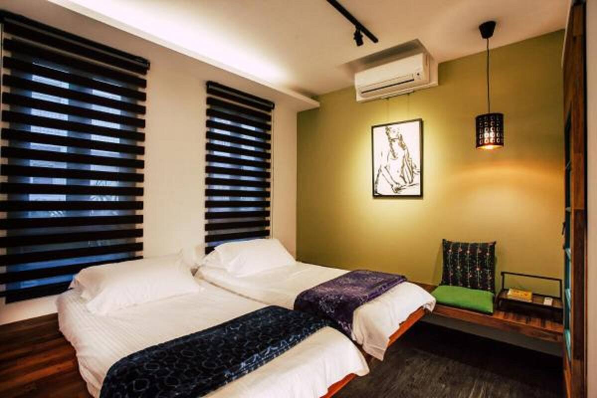 Quarto de hotel com duas camas, ar condicionado fixado na parede, uma obra de arte emoldurada e luminária pendente.