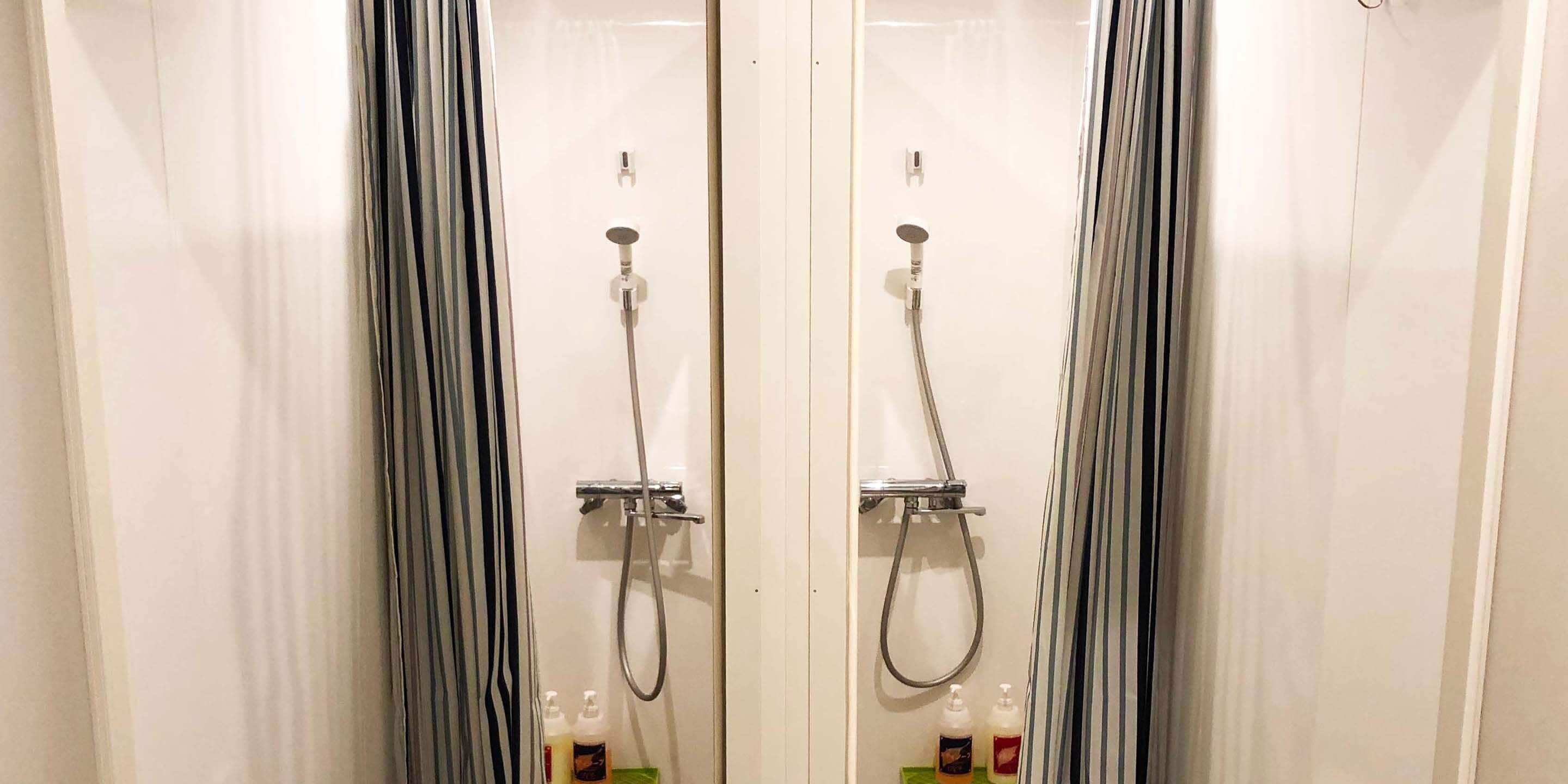 Um banheiro com dois boxes de chuveiro, cada um com chuveiro manual e torneira fixa na parede.