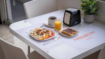Uma mesa de café da manhã com um prato de comida, uma xícara de café, um copo de suco de laranja, uma torradeira e um vaso de planta.