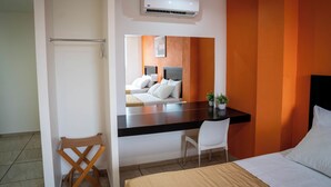 Quarto de hotel moderno com cama, escrivaninha, cadeira, mesinha de centro, ar condicionado e espelho.