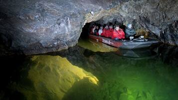 Um grupo de pessoas em um barco dentro de uma caverna com teto rochoso e água esverdeada.