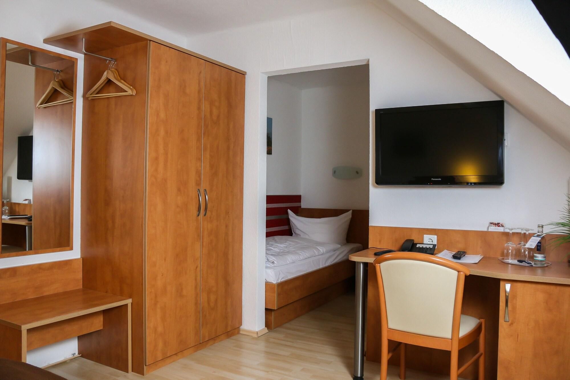 Quarto com cama, escrivaninha, cadeira, guarda-roupa e televisão na parede.