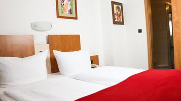 Quarto de hotel com cama, roupa de cama branca, manta vermelha e duas obras de arte emolduradas na parede.