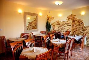 Um restaurante com várias mesas e cadeiras de madeira, uma parede decorativa com padrão de pedra e um lustre.