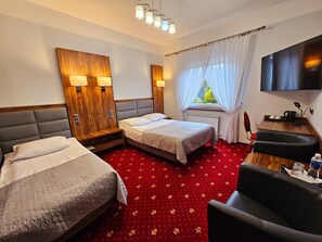 Quarto de hotel com duas camas, uma escrivaninha, uma cadeira, televisão e janela com cortinas.