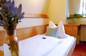 Quarto com cabeceira de madeira, roupa de cama branca e um vaso com flores.