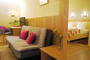 Quarto de hotel com sofá, mesa de cabeceira, televisão e cama com roupa de cama florida.