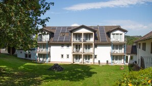 Um edifício grande de dois andares com várias varandas, painéis solares no telhado e um gramado bem cuidado.