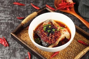 Uma tigela de sopa com peixe, decorada com ervas verdes, sobre um tabuleiro de palha.