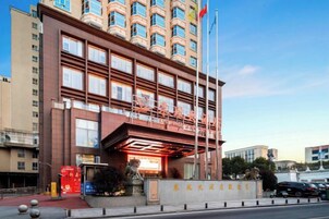 Um hotel com vários andares, uma entrada destacada, uma bandeira e uma estátua em frente.