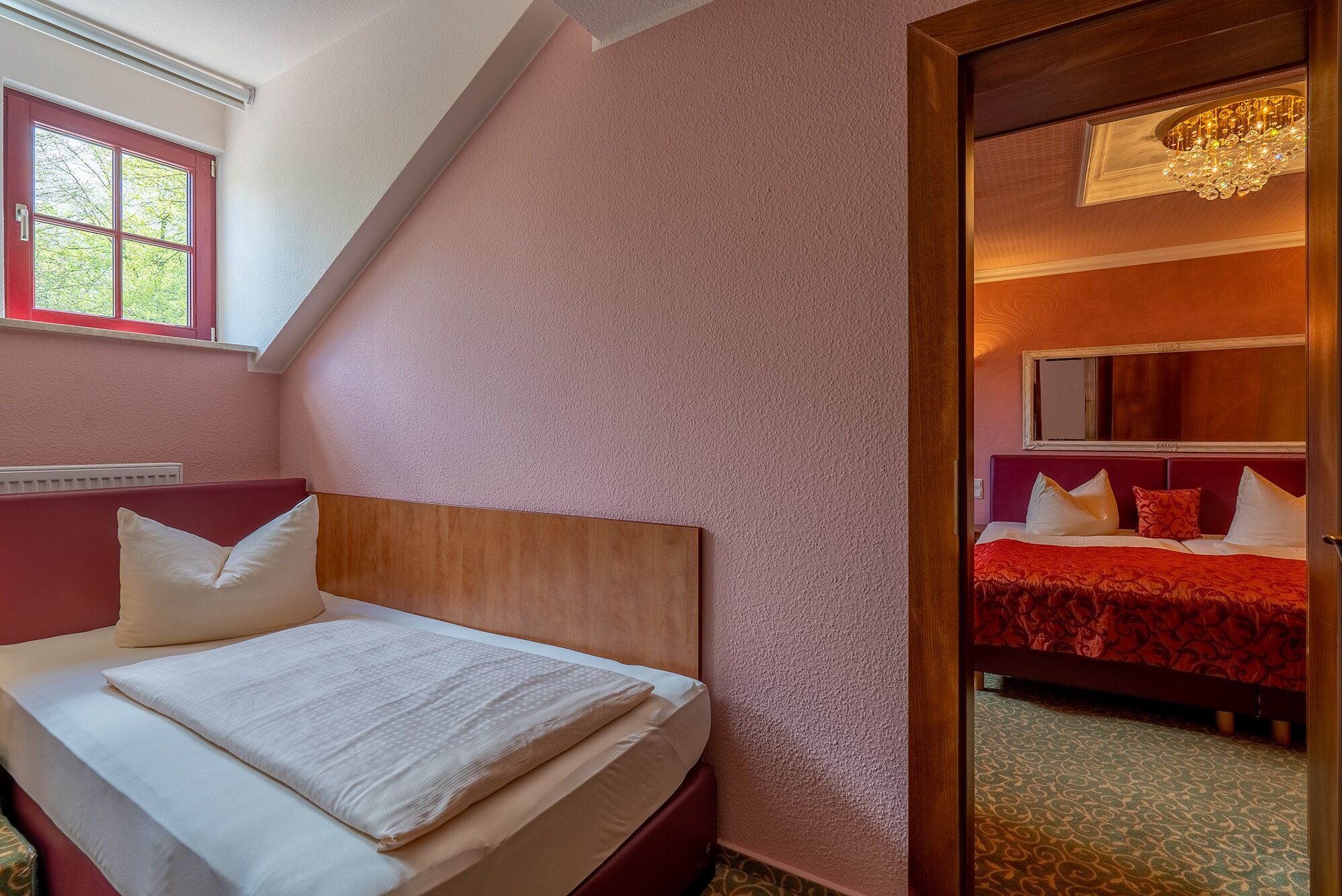 Quarto com cabeceira de madeira, uma janela grande com moldura vermelha e um espelho sobre a cama.