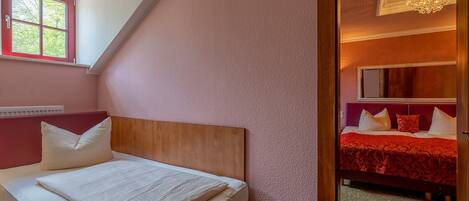 Quarto com cabeceira de madeira, uma janela grande com moldura vermelha e um espelho sobre a cama.