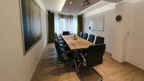 Uma sala de conferências com uma mesa comprida, cadeiras pretas, um projetor e um relógio na parede.