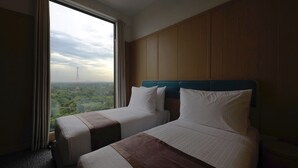 Quarto de hotel com duas camas, uma janela grande com cortinas e vista para a paisagem urbana.