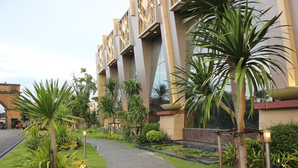 Uma trilha bordeada por plantas tropicais que leva a um edifício moderno com arquitetura geométrica.