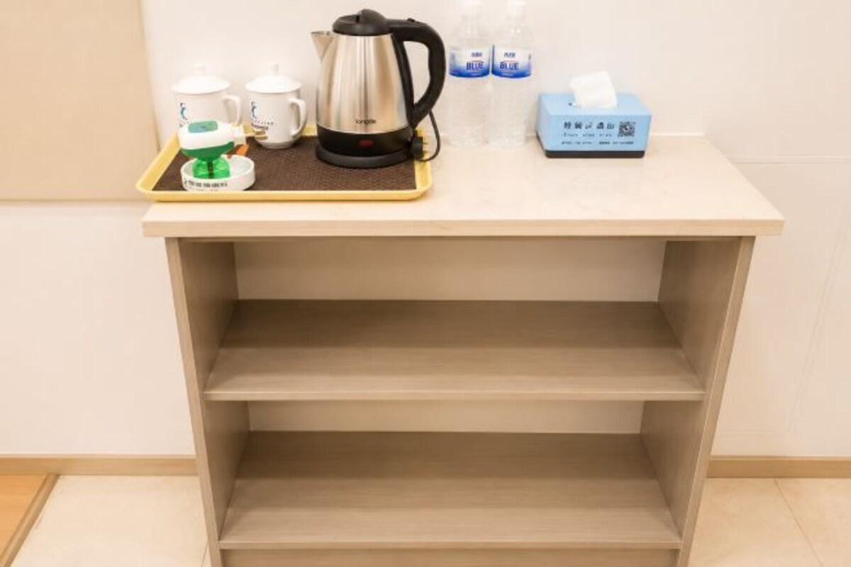 Quarto de hotel com mesa de madeira, cafeteira, xícaras e um suporte.