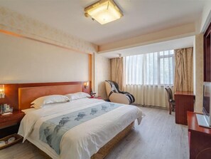 Quarto de hotel com uma cama grande, escrivaninha, cadeira, um violão e televisão.