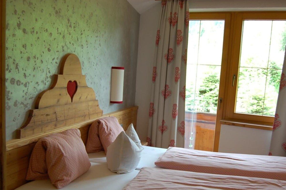 Um quarto com cama de madeira, cabeceira com recorte em formato de coração e janela com cortinas.